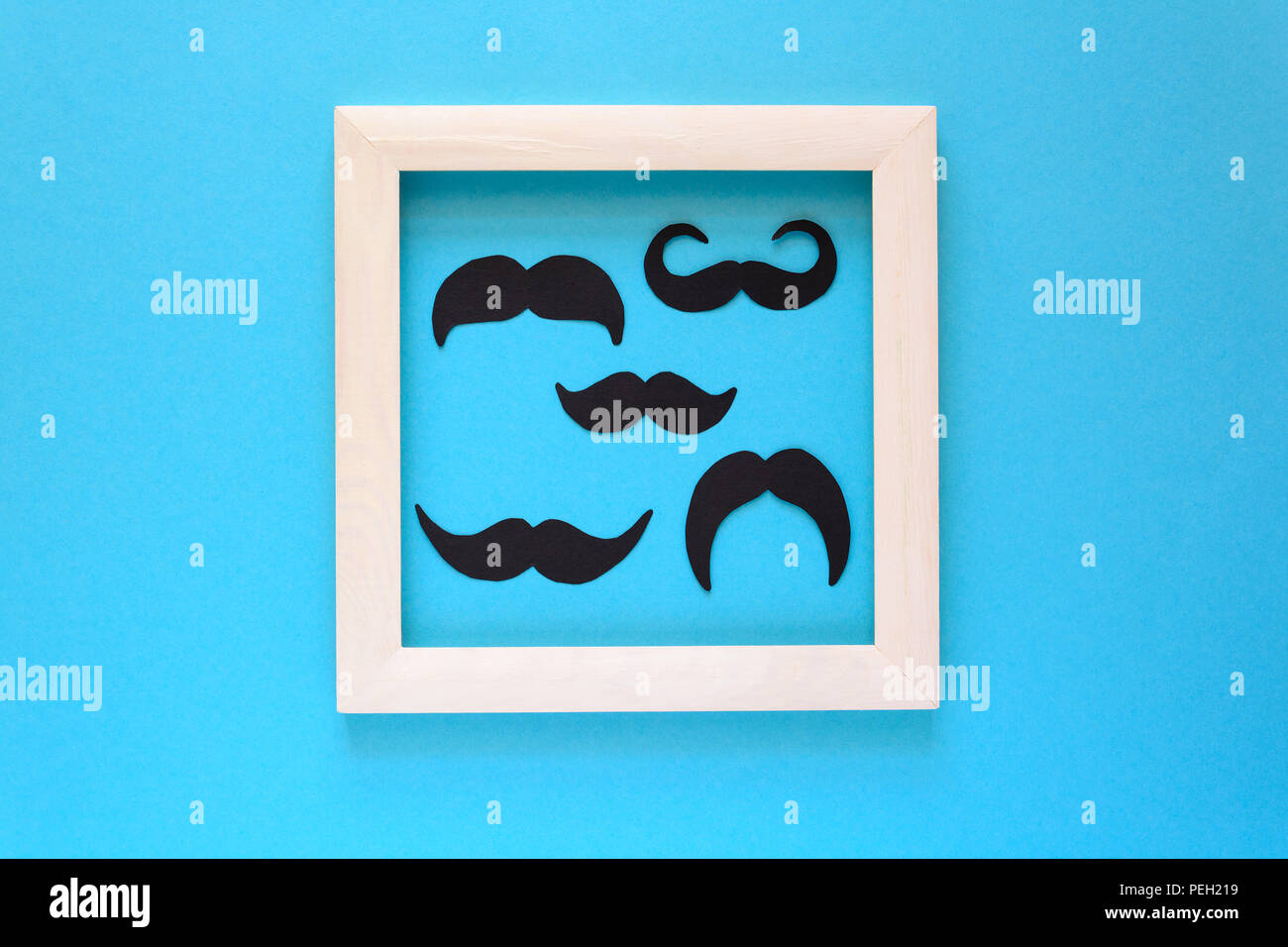 Paper moustache into white wooden frame on blue paper background. Cut ...