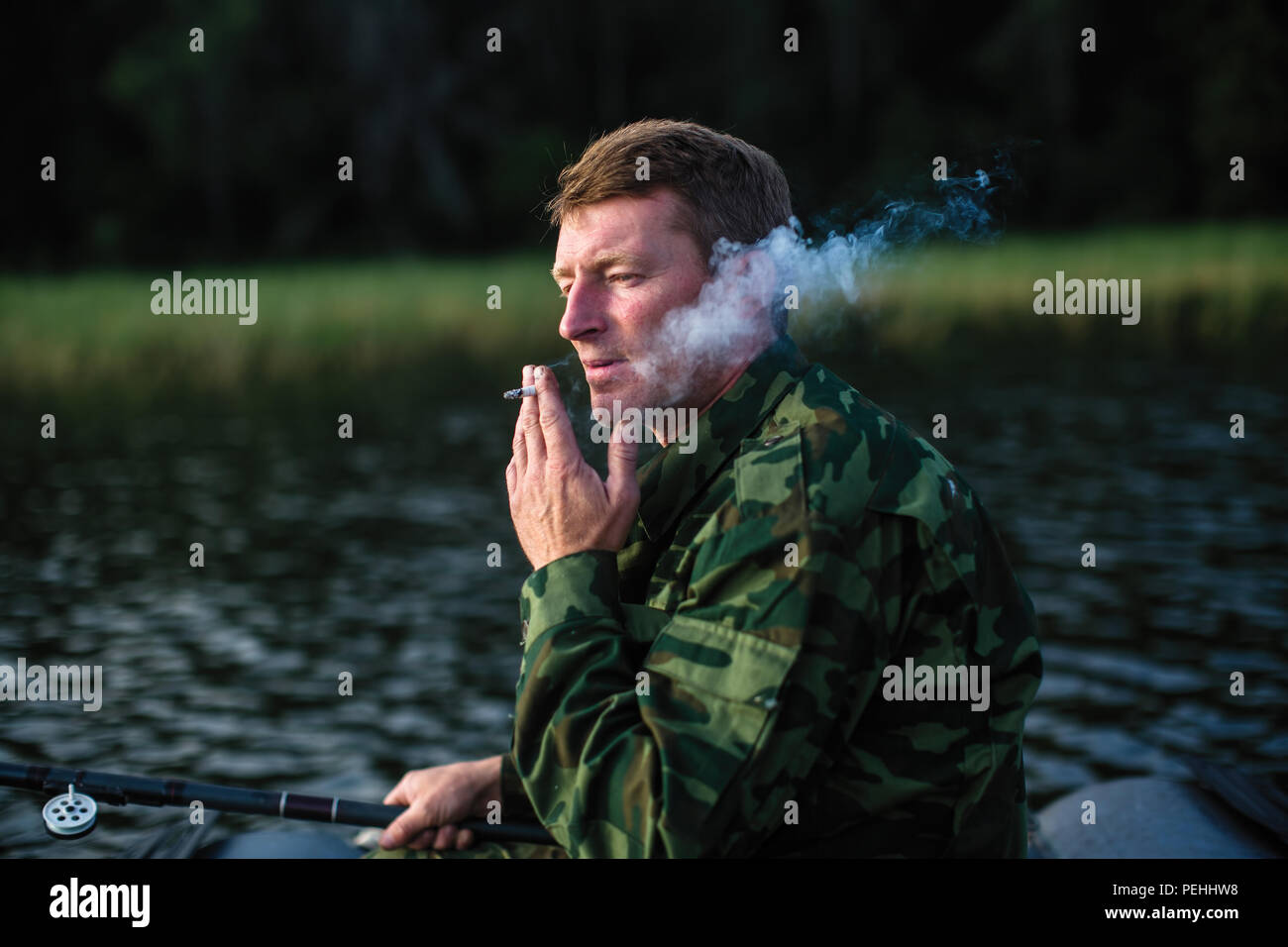 Fisherman in camouflage smoking a cigarette on a rubber boat in the ...