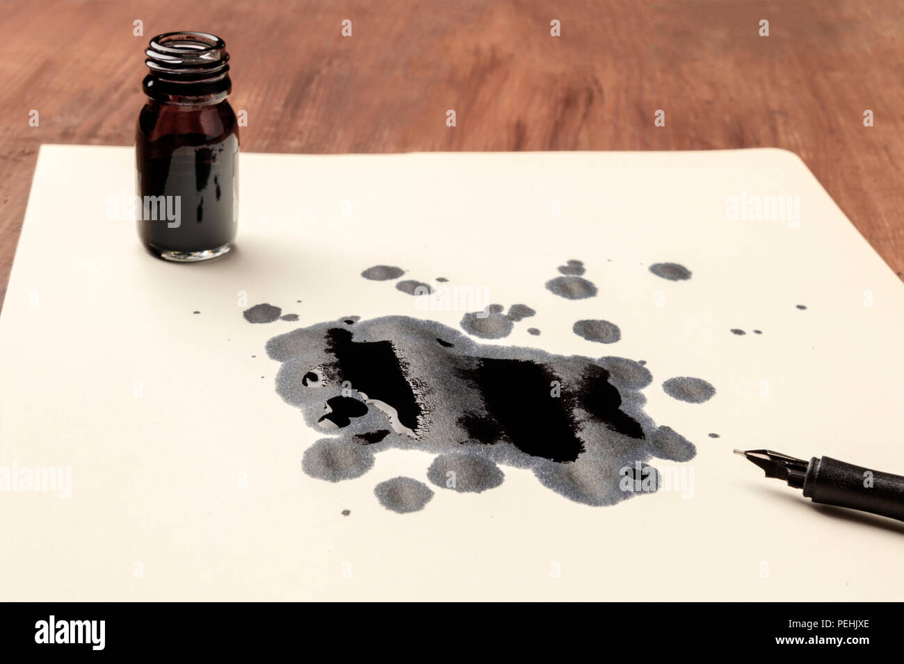 A photo of drops of ink on paper, an ink well and and a nib pen, with ...