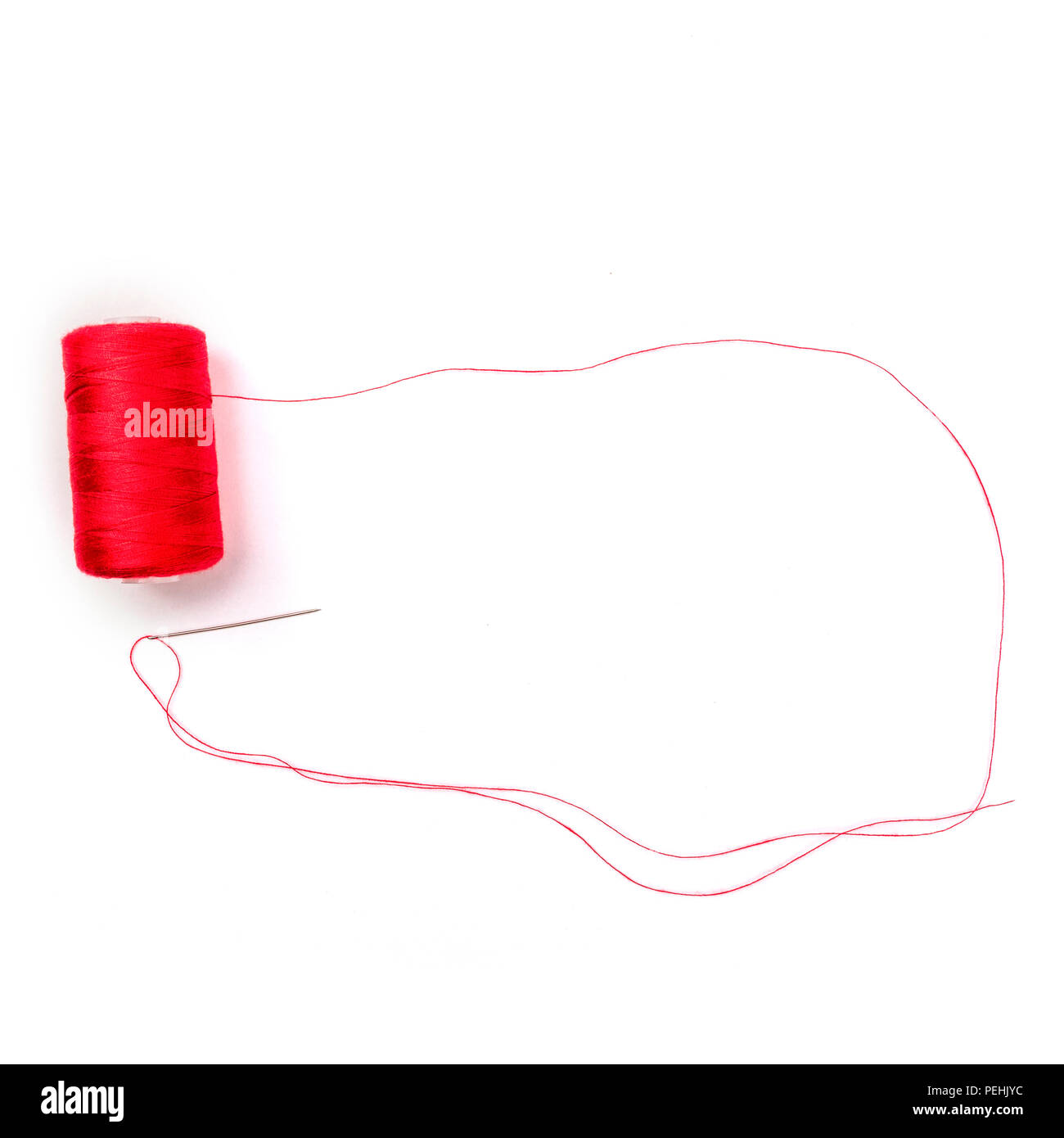 Overhead photo of a needle with a red thread and a spool on a white ...