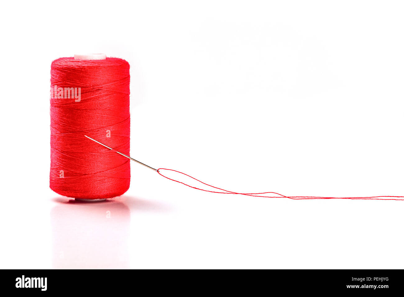A photo of a needle with a red thread and a spool on a white background ...