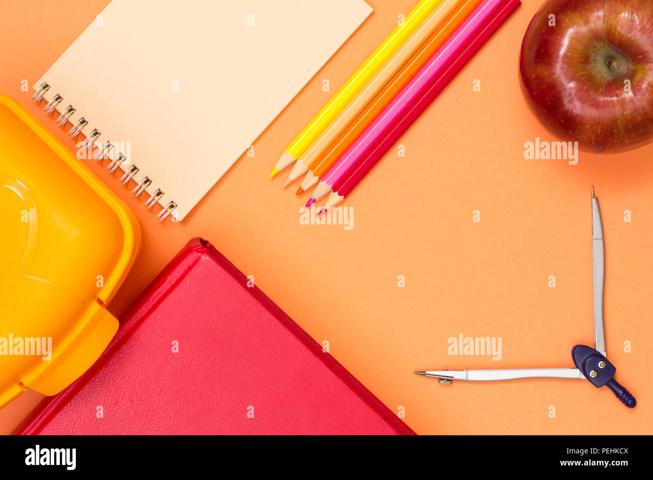 Book, lunch box, notebook, color pencils, apple and compass on pink ...