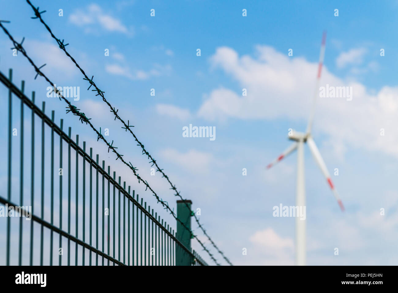 renewable energy concept: wind turbine behind a fence against great ...