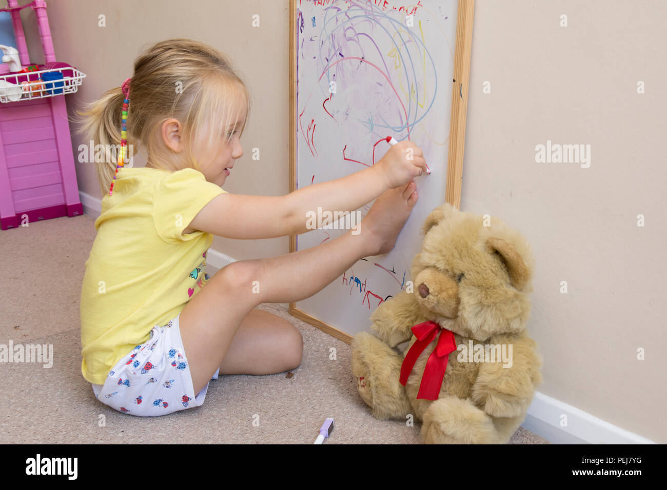 young two year old girl drawing with coloured pen on white board, being ...