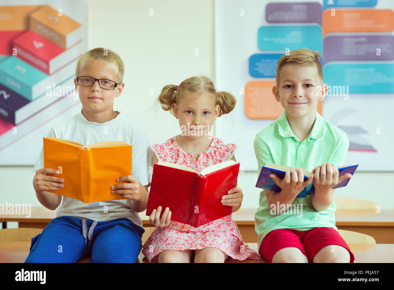 Three schoolchildren reading books in classroom at school Stock Photo ...