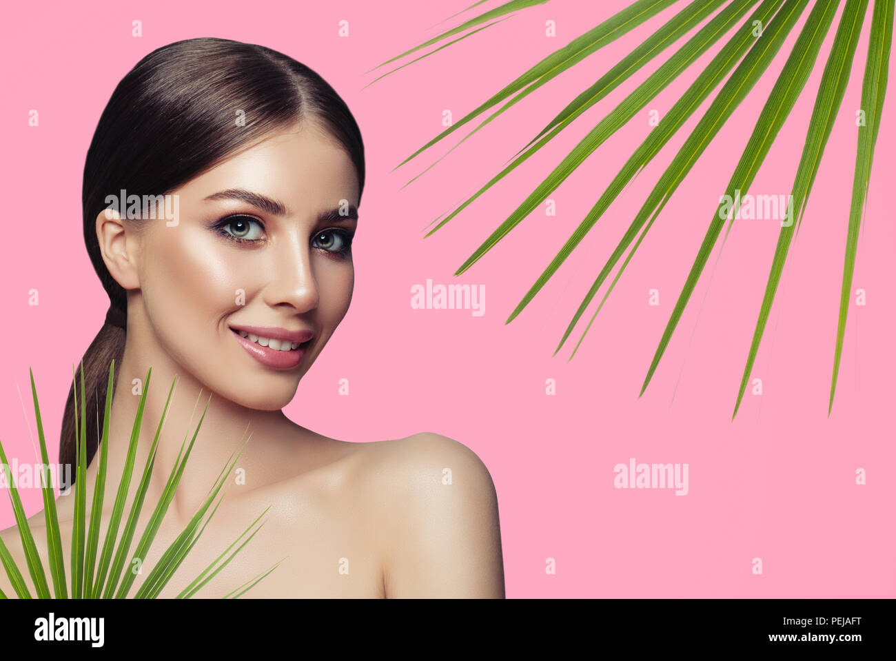 Young spa model with green leaves on pink background with copy space ...