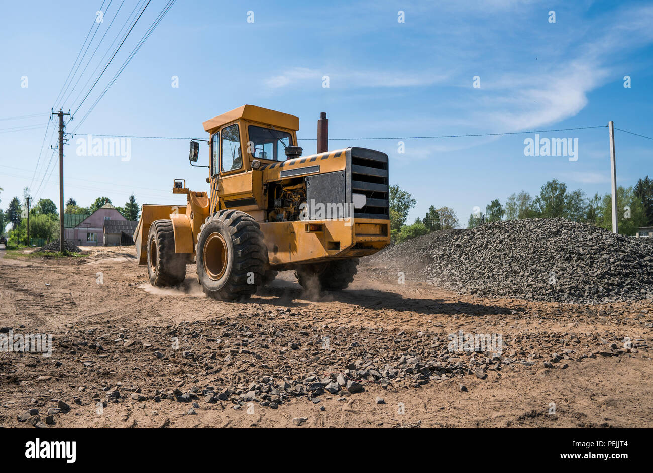 Yellow loader moving with uploaded bucket with stone gravel during road ...