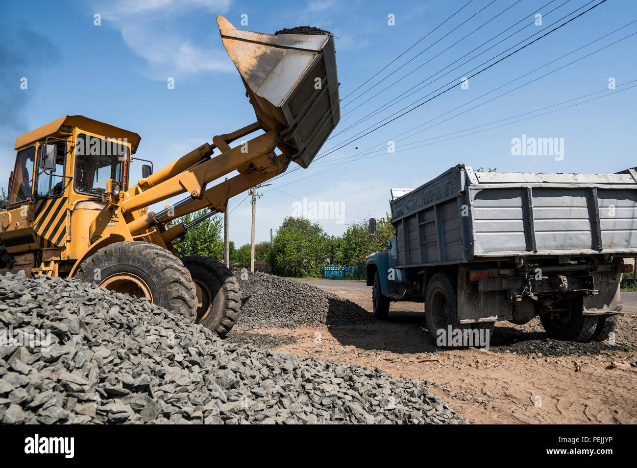 Yellow loader delivering stone gravel into truck during road ...