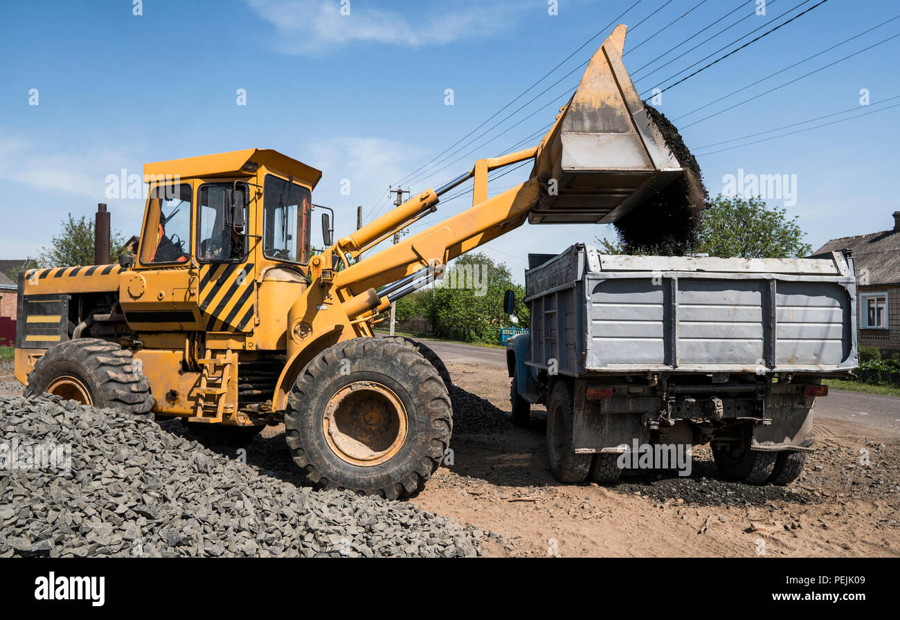 Yellow loader delivering stone gravel into truck during road ...