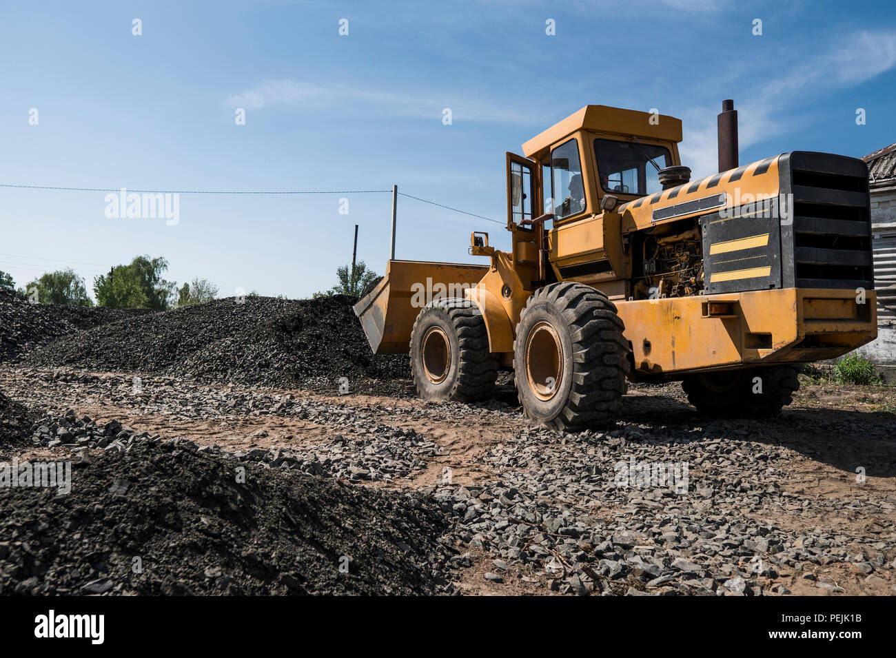 Yellow loader moving with uploaded bucket with stone gravel during road ...