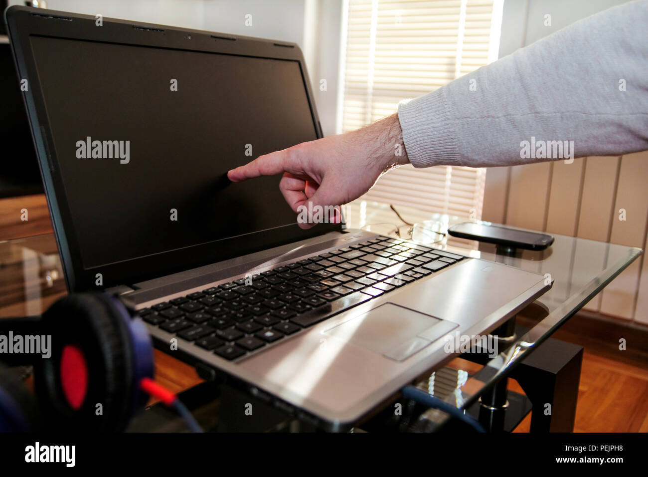 Male hand forefinger about to tap a laptop screen indoor. With his ...