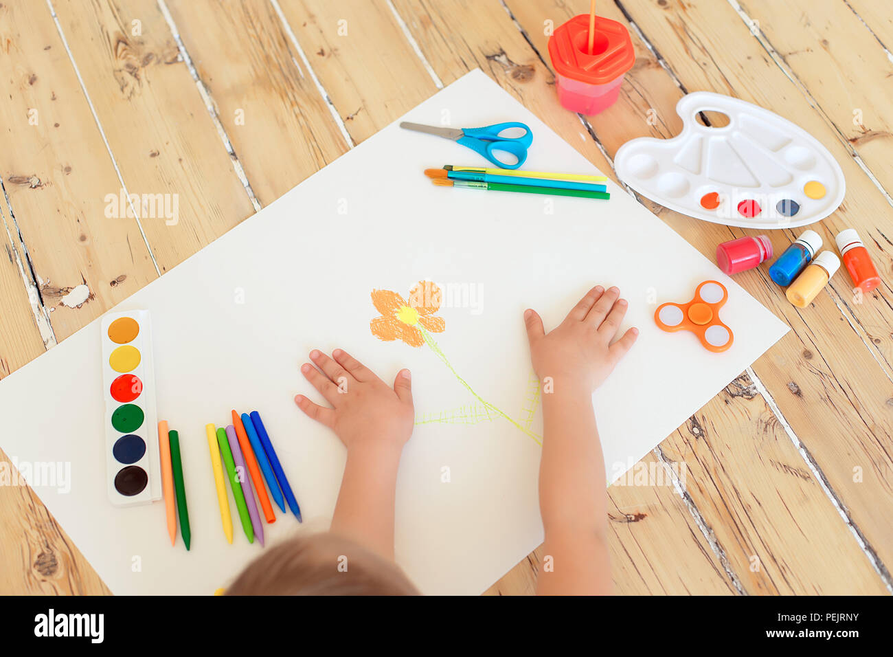Little blonde girl painting on big white paper while laying on the ...