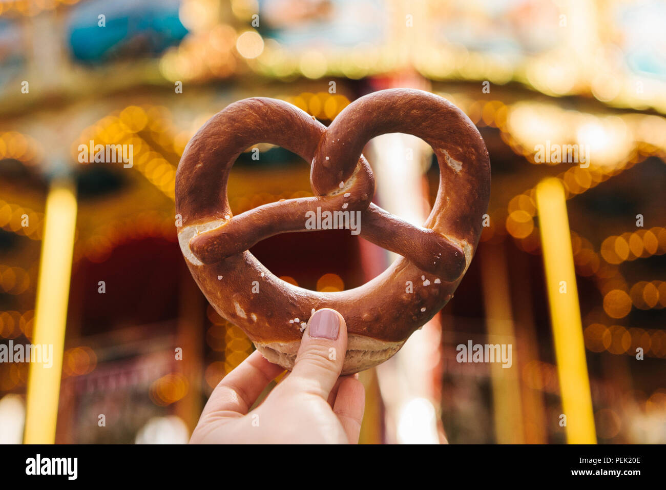 The girl is holding a traditional German pretzel. Carousel or merry-go ...
