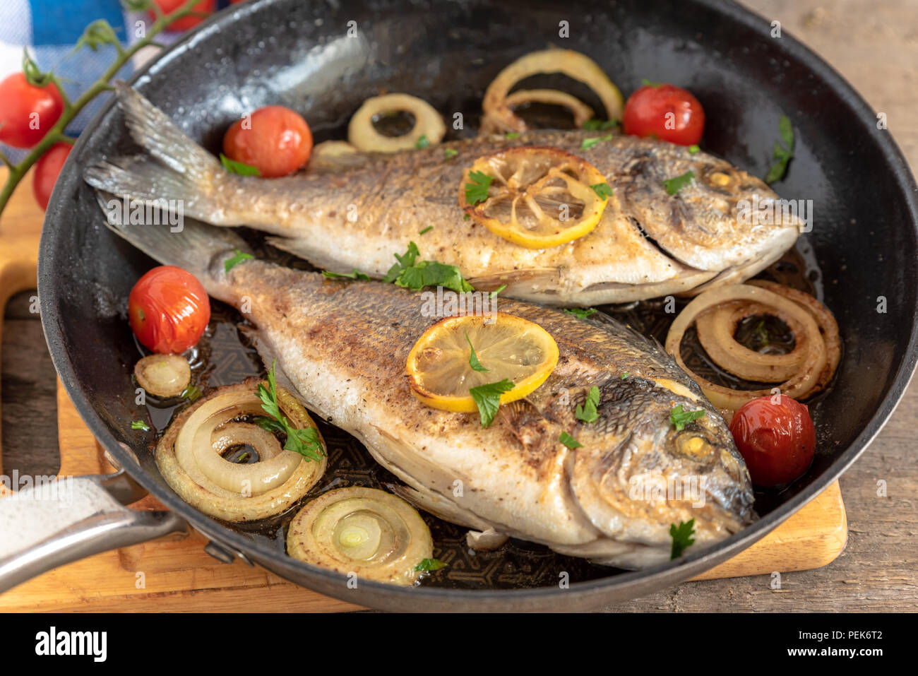 Dorada fried in a pan with onions, lemon and cherry tomatoes Stock ...