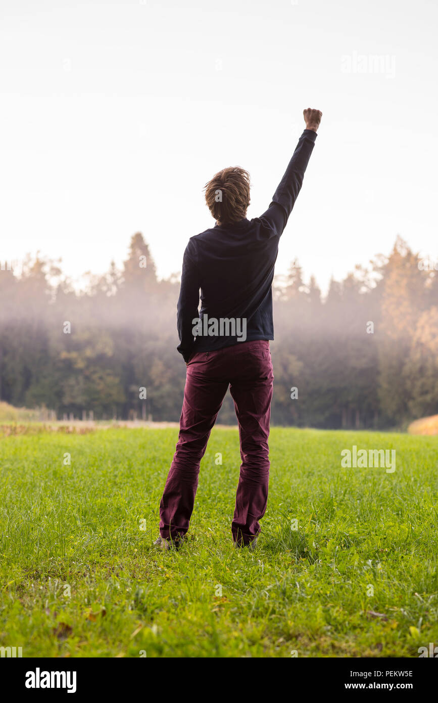 Rear view of a man standing in green meadow with one arm lifted in the ...