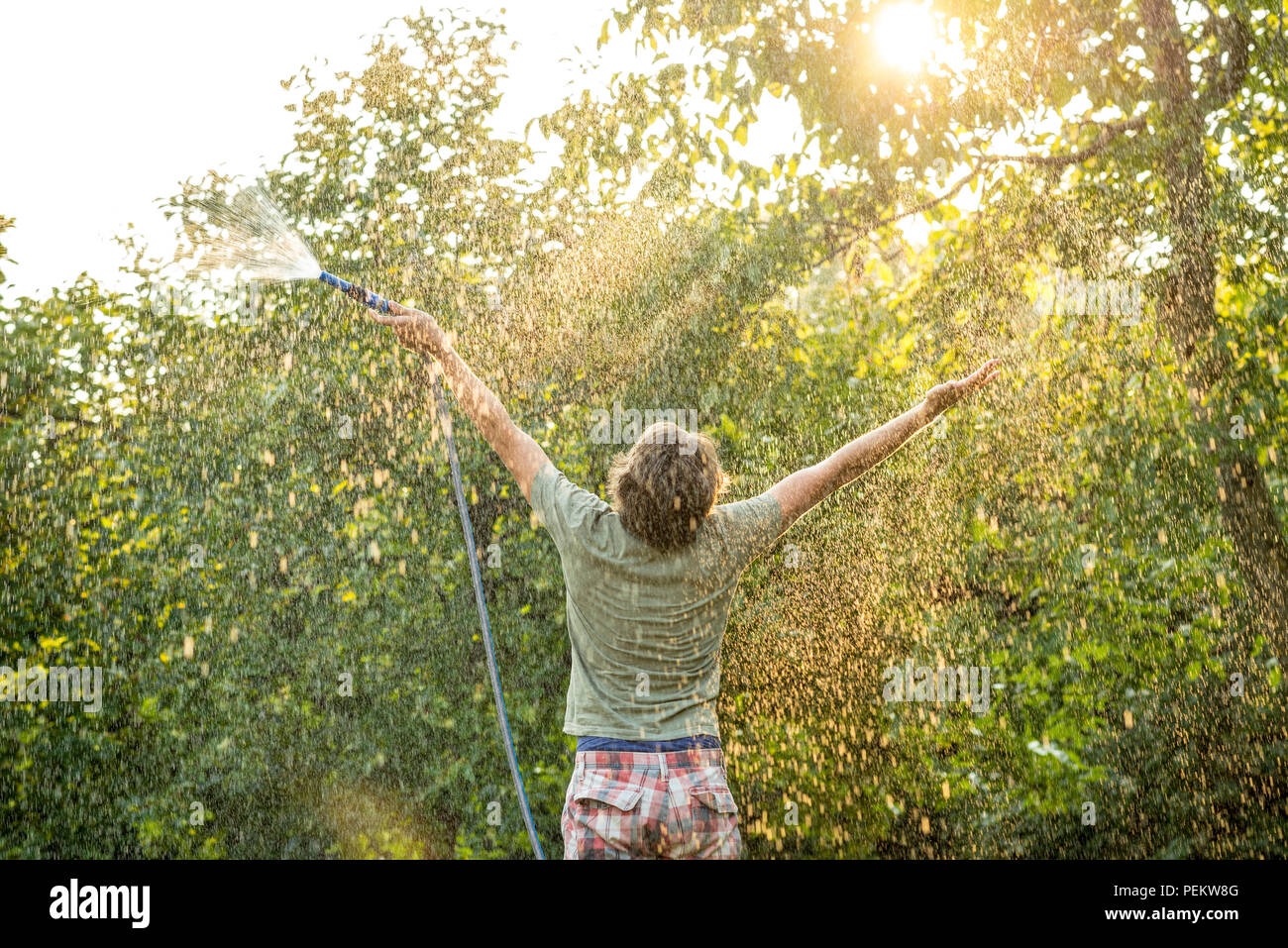 Three-Quarter Rear View Shot of a Man Holding a Garden Hose and Raising ...