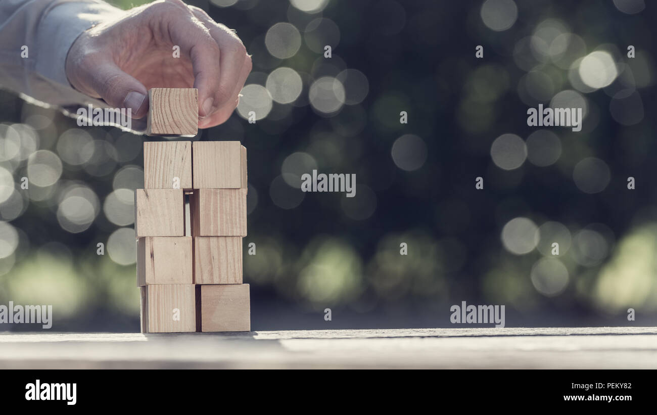 Retro toned image of man building a tower of blank wooden blocks ...