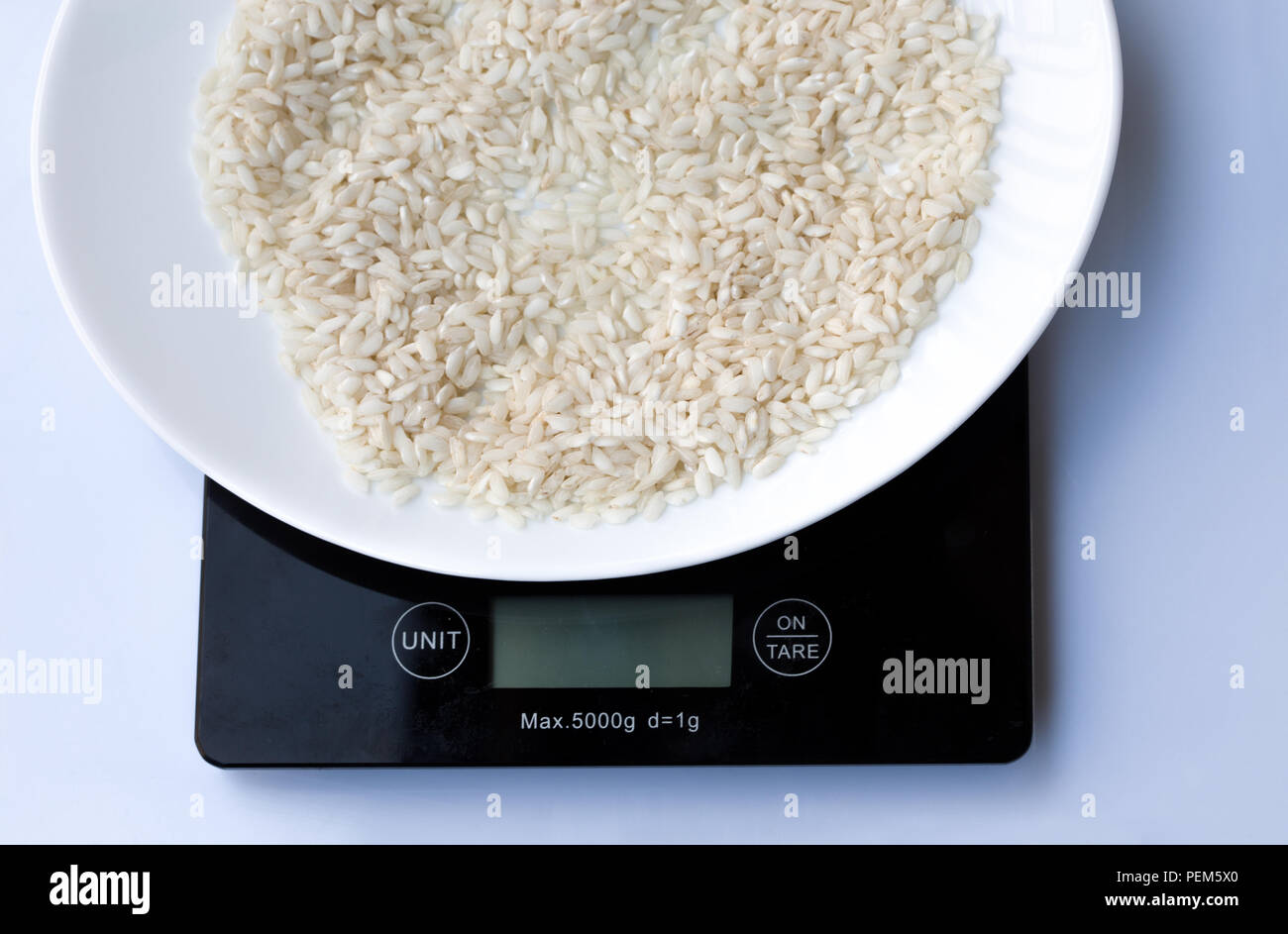 Raw italian rice in a white plate on a black weight scale on a white ...