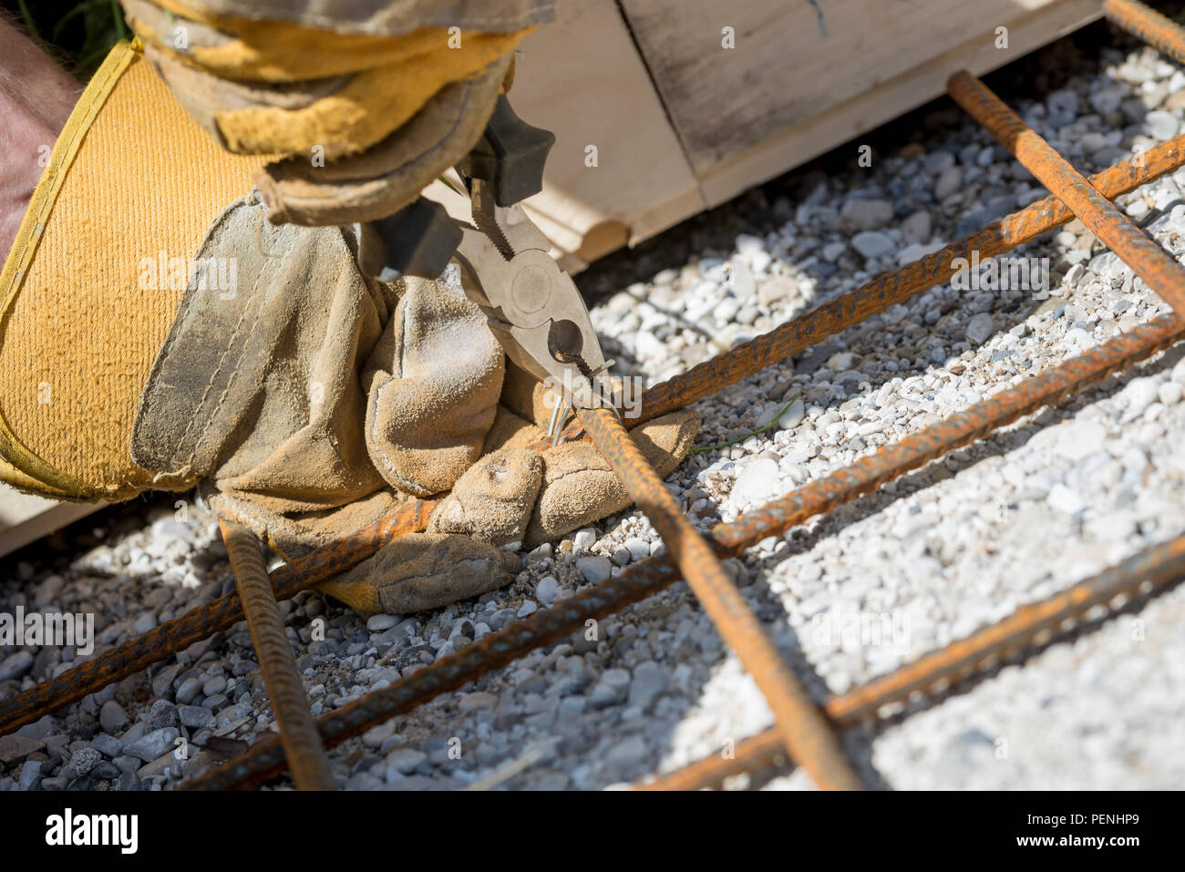 Worker tying steel reinforcing rods with string to position them over a ...
