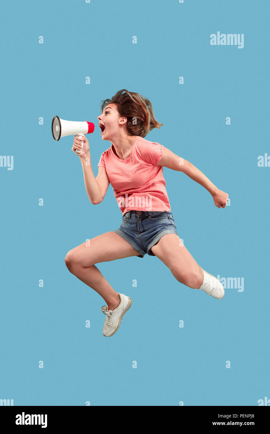 Beautiful young woman jumping with megaphone isolated over blue ...