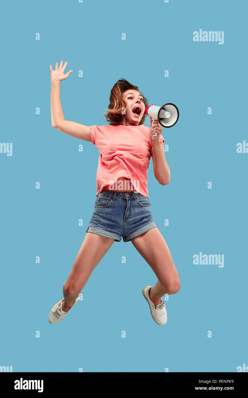 Beautiful young woman jumping with megaphone isolated over blue ...