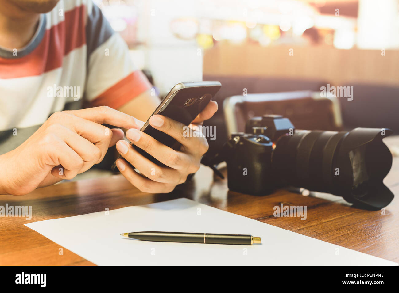 Man's hands using smart phone with DSLR camera and pen over paperwork ...