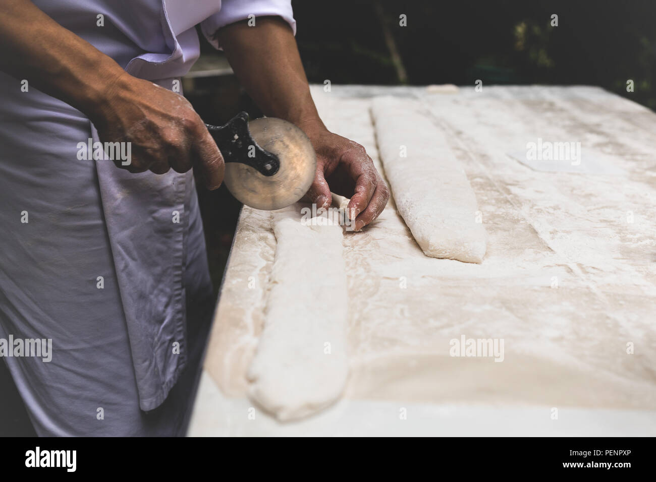 Chef cutting a pastry with pizza knife on table top in matte color ...