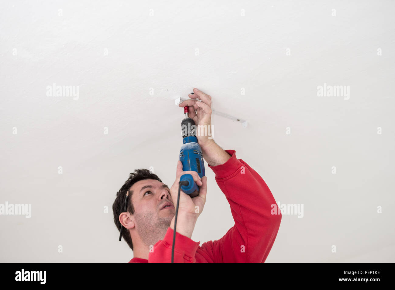Builder using a small handheld electric drill to drill a hole in the ...