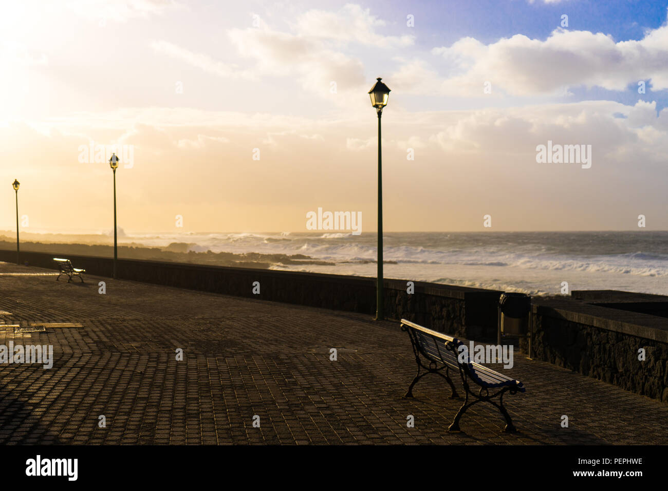 Lamp posts along beachside walkway with view of ocean and sky at sunset ...