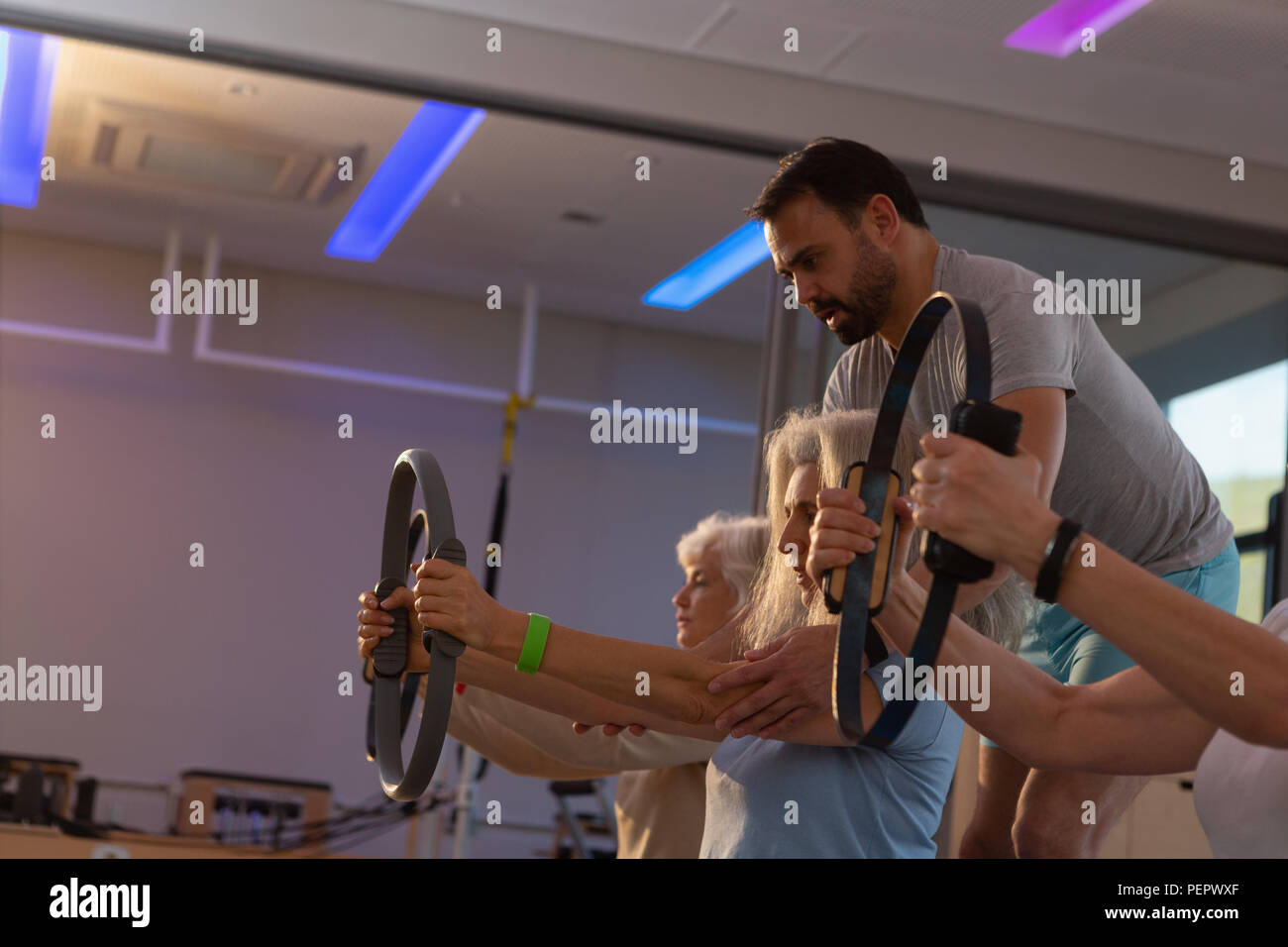 Trainer assisting senior women in performing yoga Stock Photo - Alamy