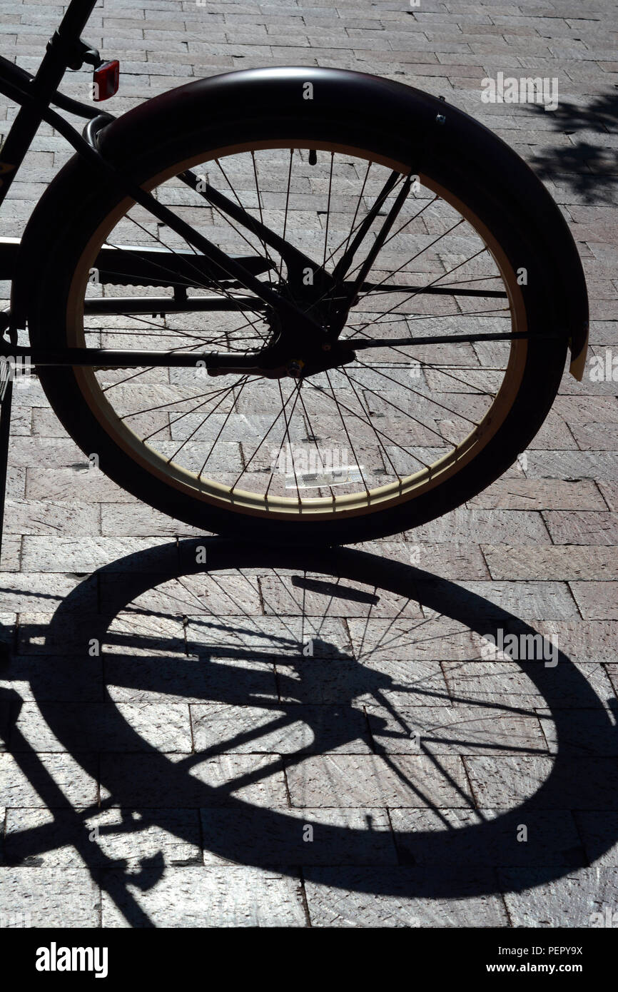 A bicycle wheel casts a shadow on a sidewalk Stock Photo - Alamy