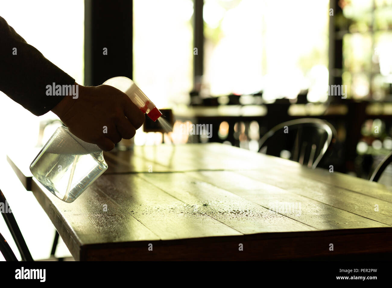 Silhouette waiter cleaning the table with disinfectant spray in a ...