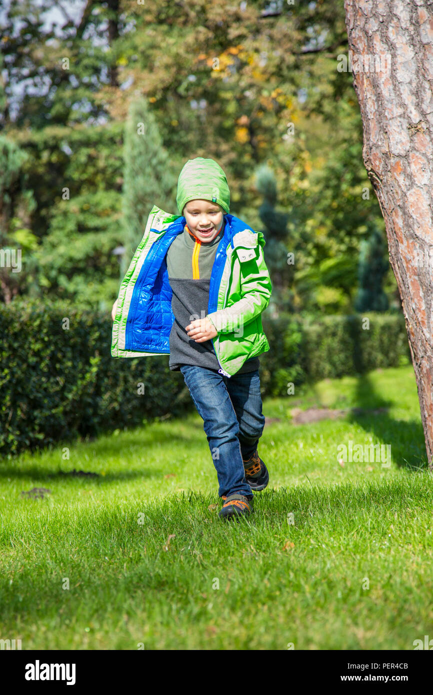 A child is running along the green grass in park in spring. Happy kid ...