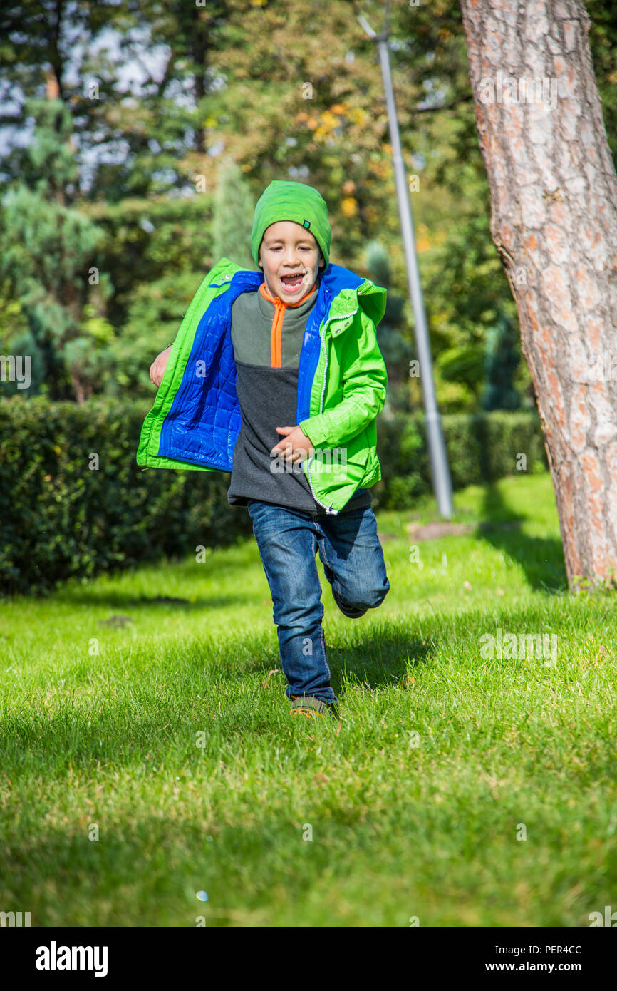 A child is running along the green grass in park in spring. Happy kid ...
