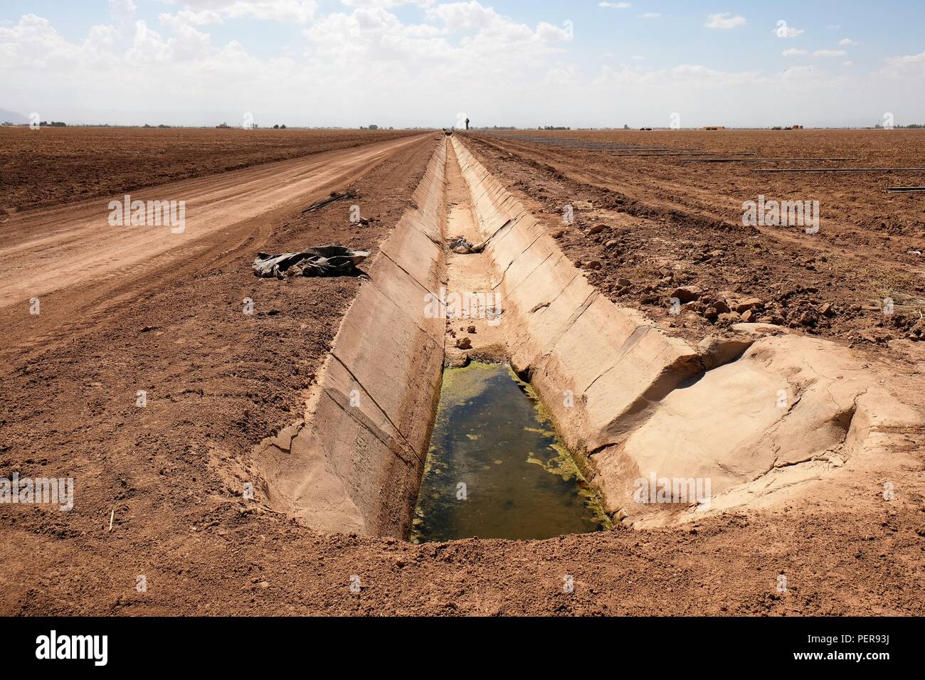 Drained irrigation canal with residual water surrounded by empty fields ...