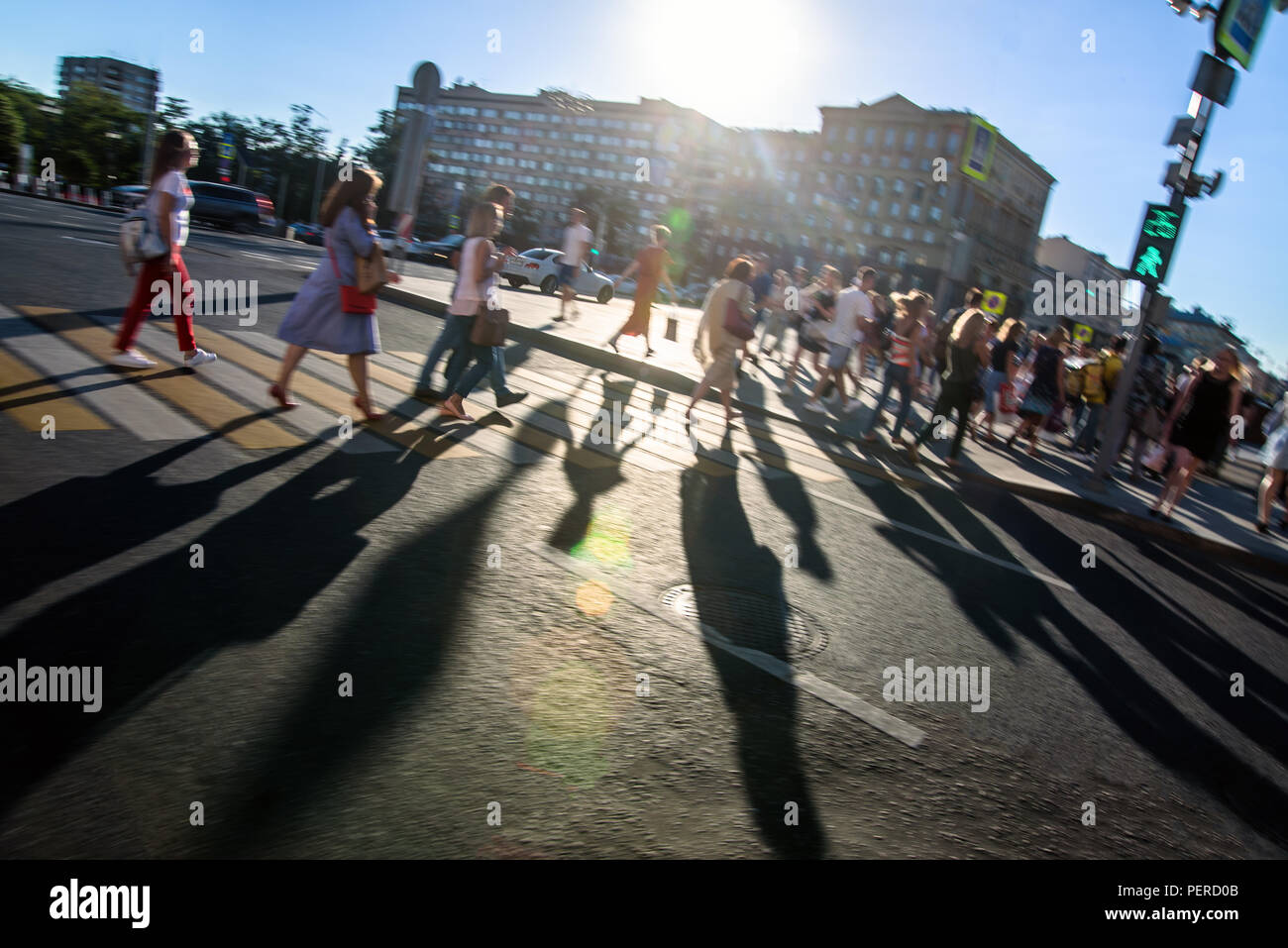 Crowd of blurred anonymous people with long shadow walking on zebra ...