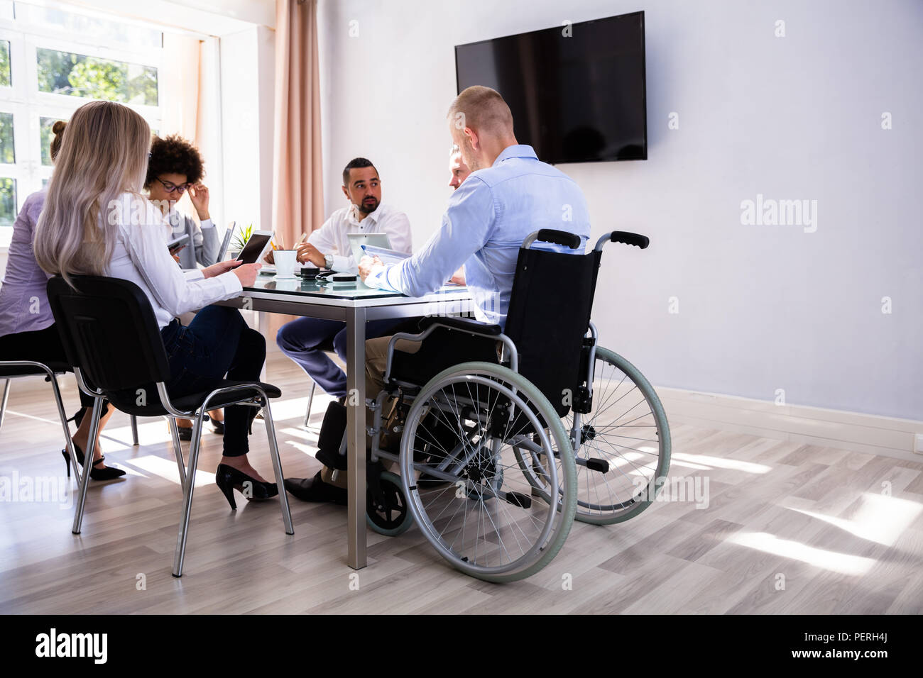 Disabled Male Manager Sitting With His Colleagues At Workplace Stock ...