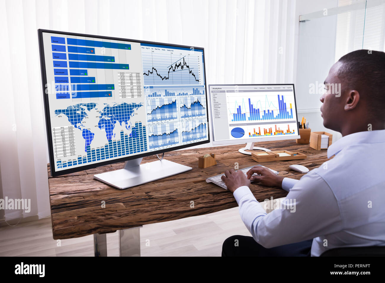 Rear View Of A Businessman Analyzing Graphs On Computers Over The ...