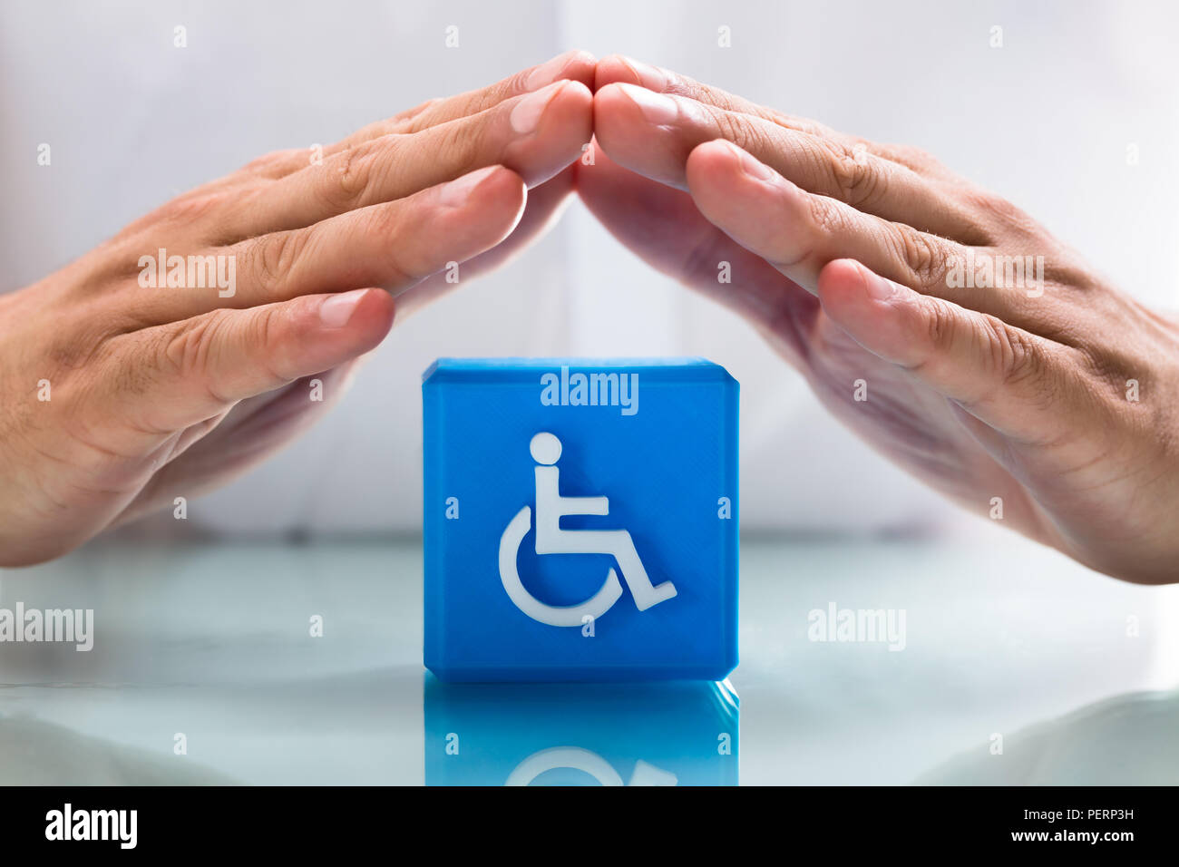 Close-up of a human hand protecting blue cubic block with handicap icon ...
