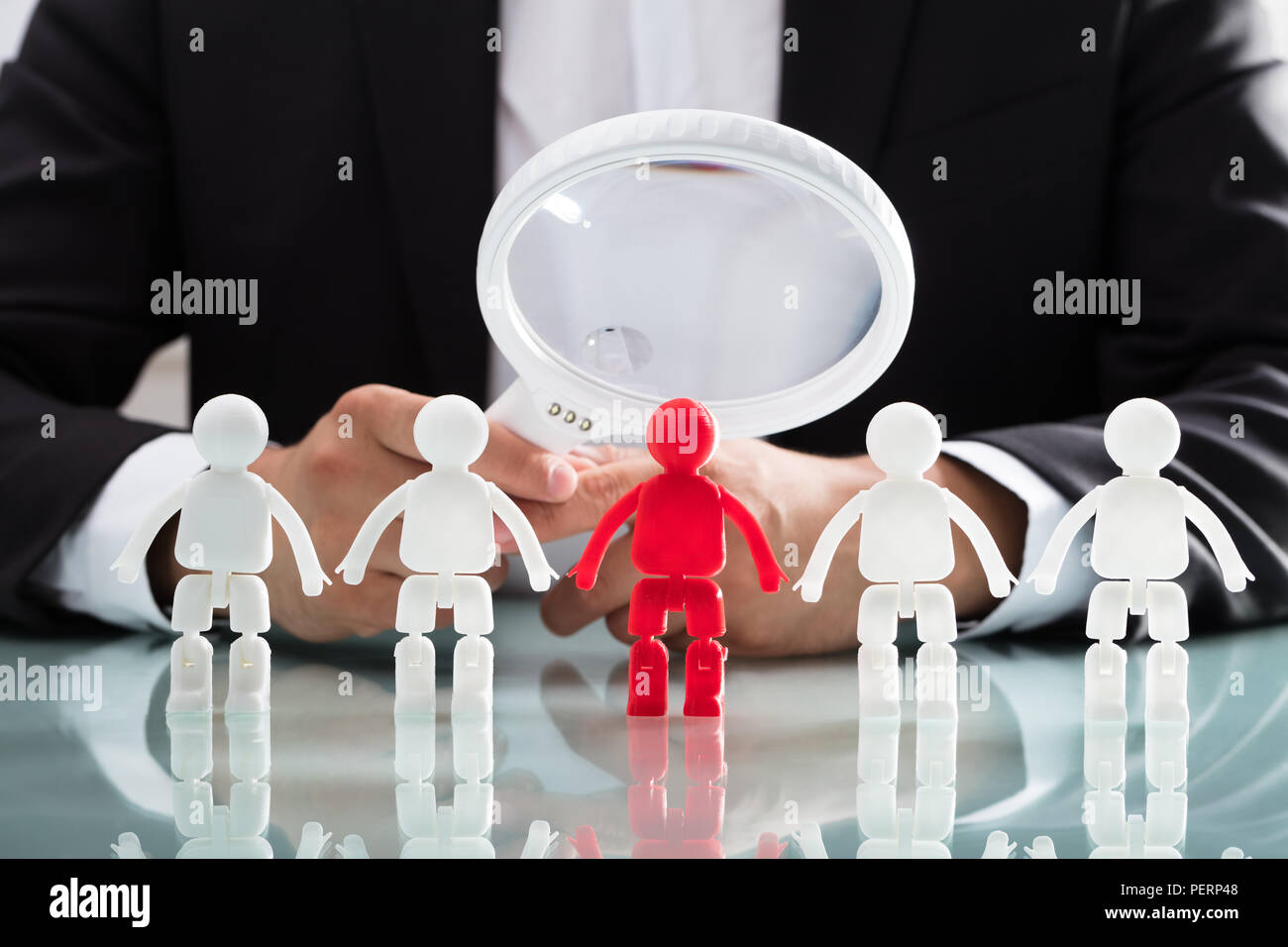 Businessperson's hand looking at red human figure through magnifying ...