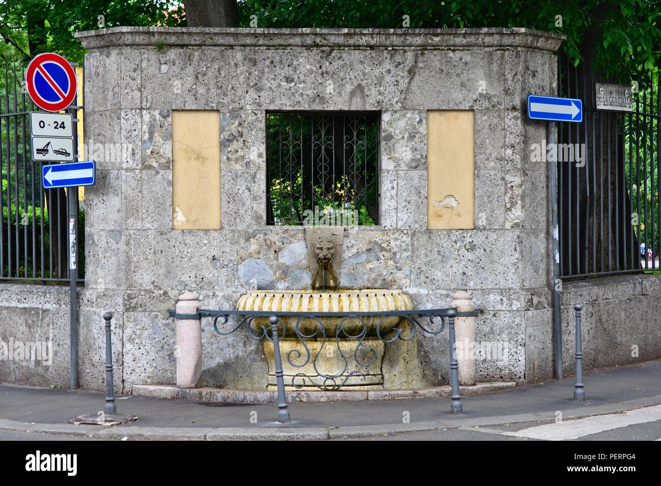 A fountain on a street corner in Milan with road signs pointing in ...