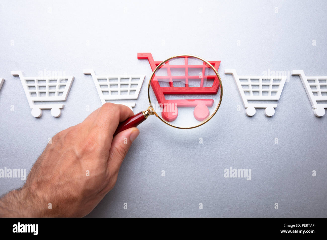 A Person Looking At Shopping Cart Through Magnifying Glass On Grey ...