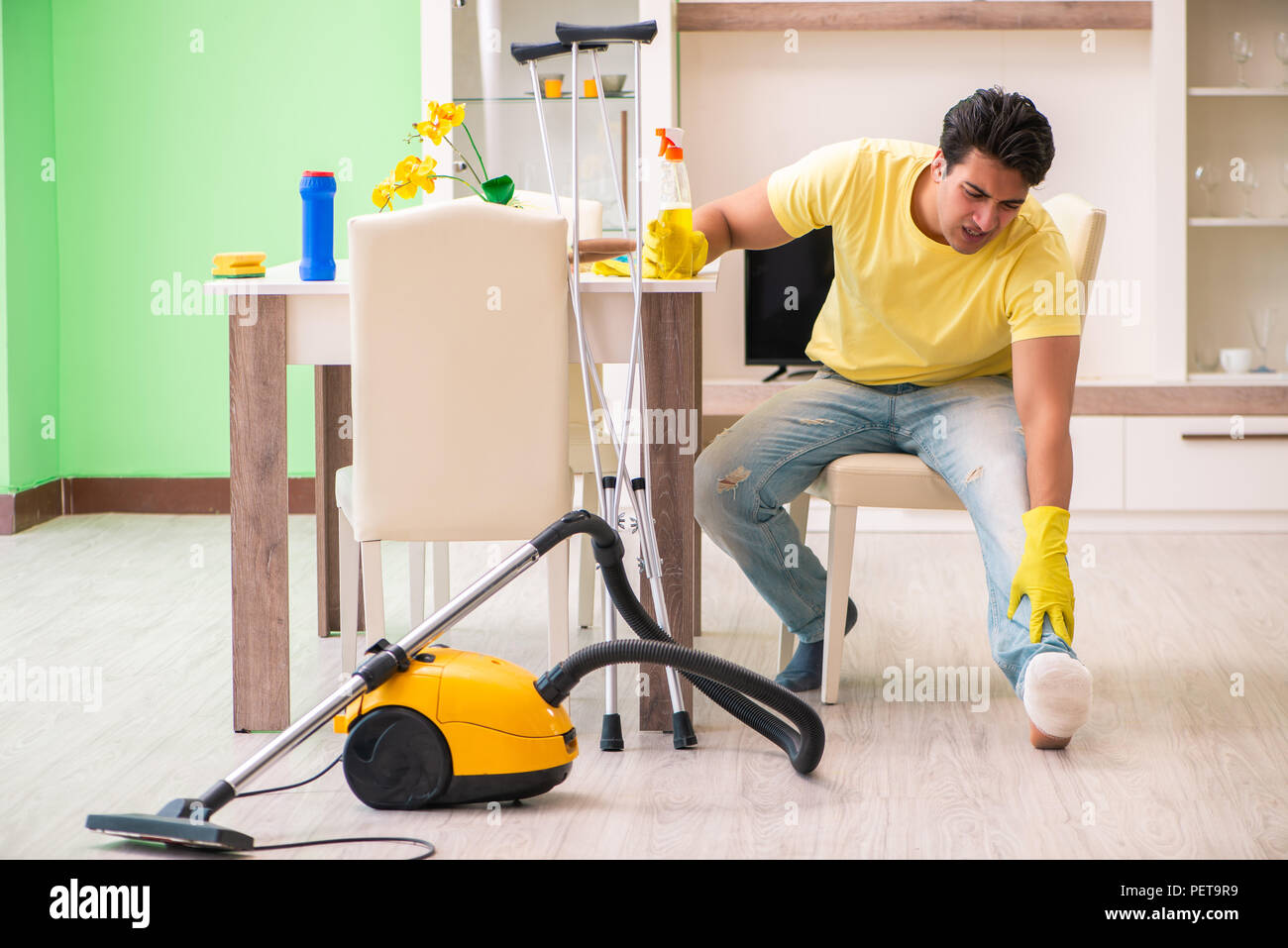 Injured man on crutches cleaning house Stock Photo - Alamy