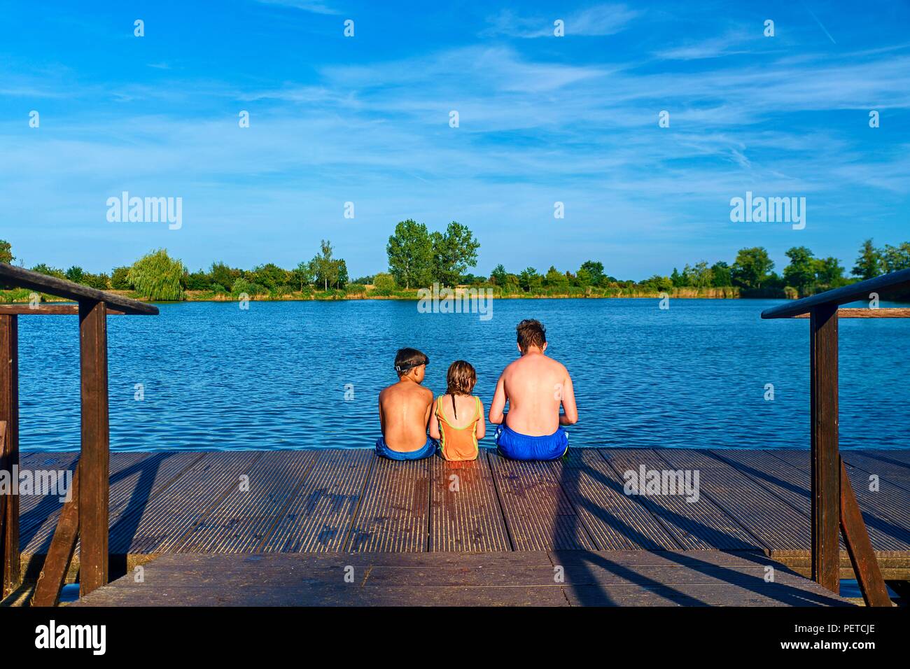 Children sitting on pier. Three children of different age - teenager ...