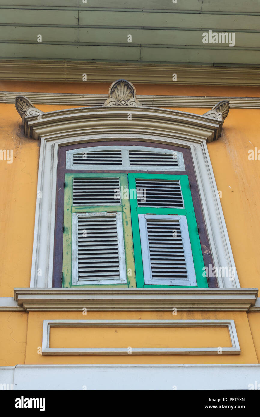 Vintage old yellow wall with green window leaves. Old dirty window on ...