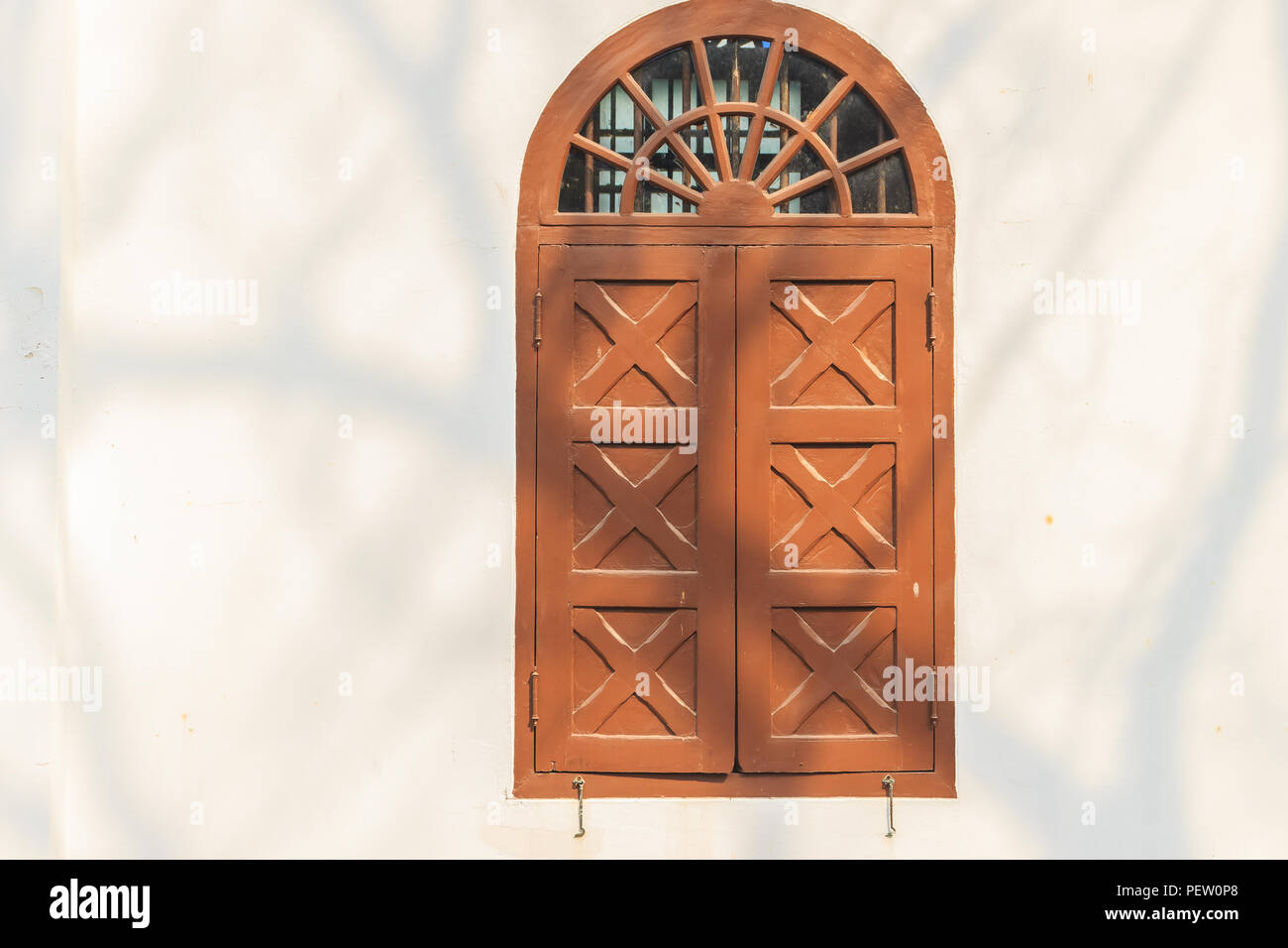 Old arched wooden window on white wall with shadows of tree branches ...