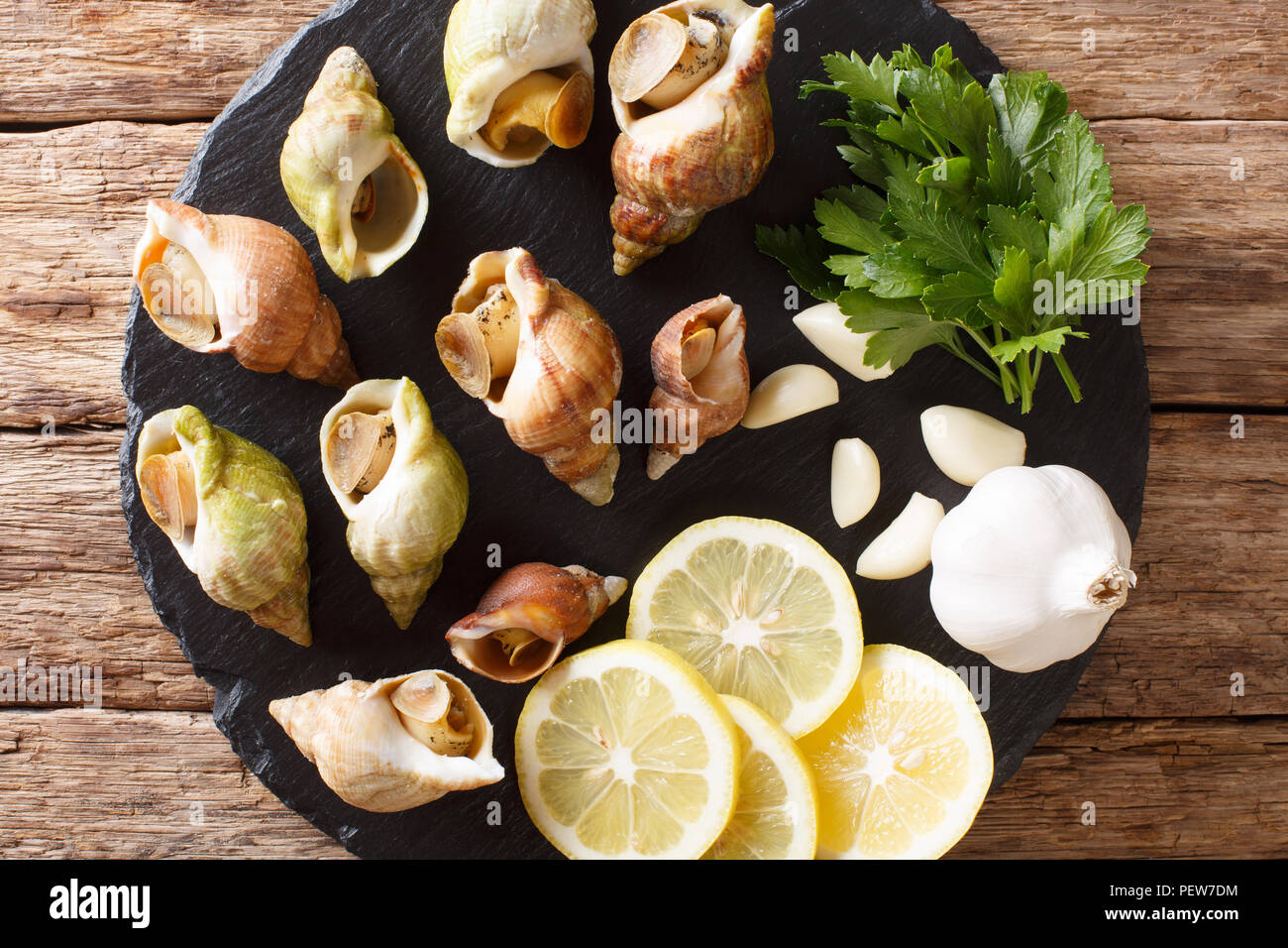 Fresh raw shellfish whelk, sea snails bulot close-up and lemon, parsley ...