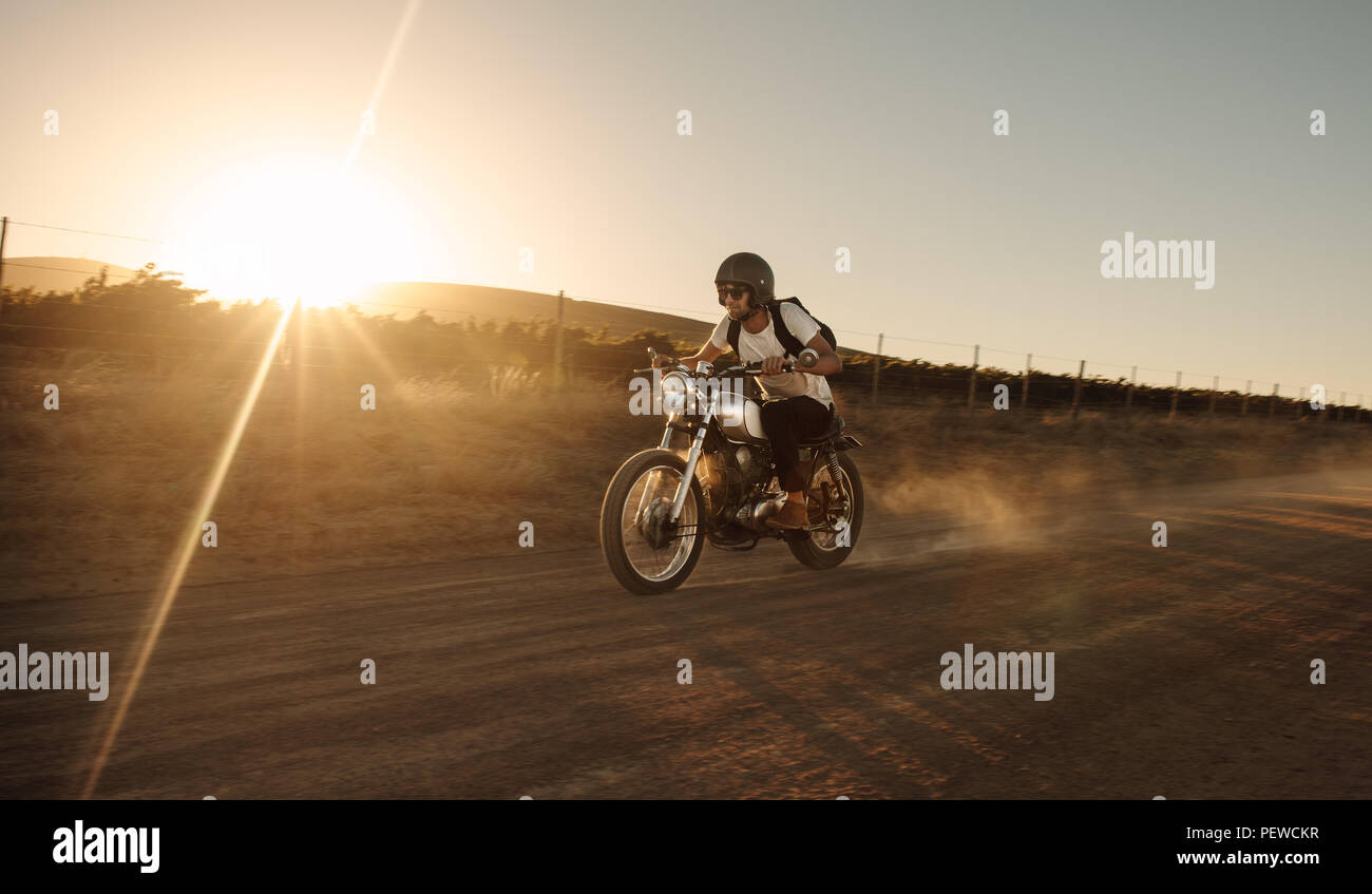 Male biker driving a vintage motorcycle on dirt road. Man riding fast ...