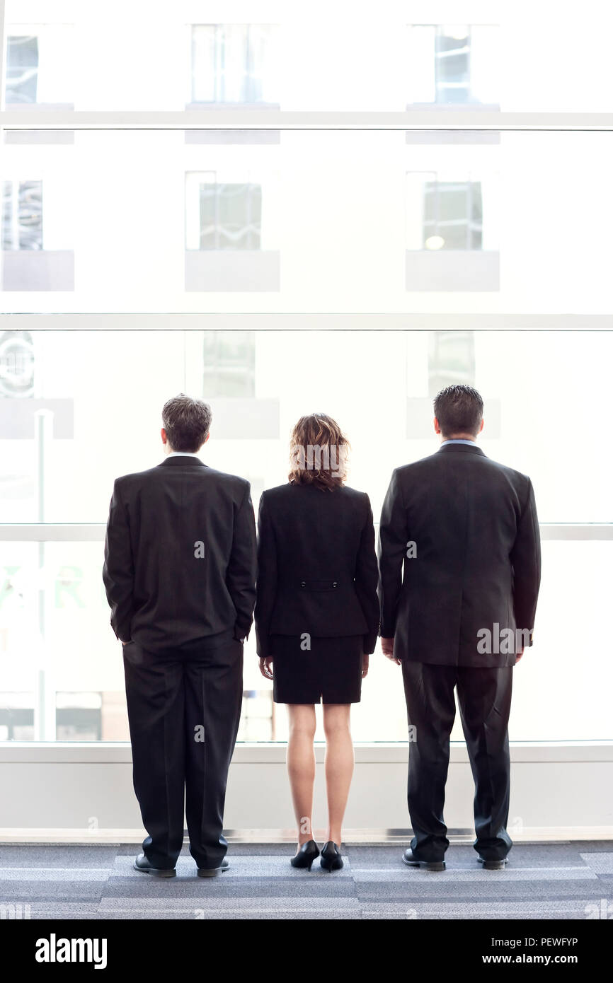 Rear view of group of three business people looking out the window of a ...