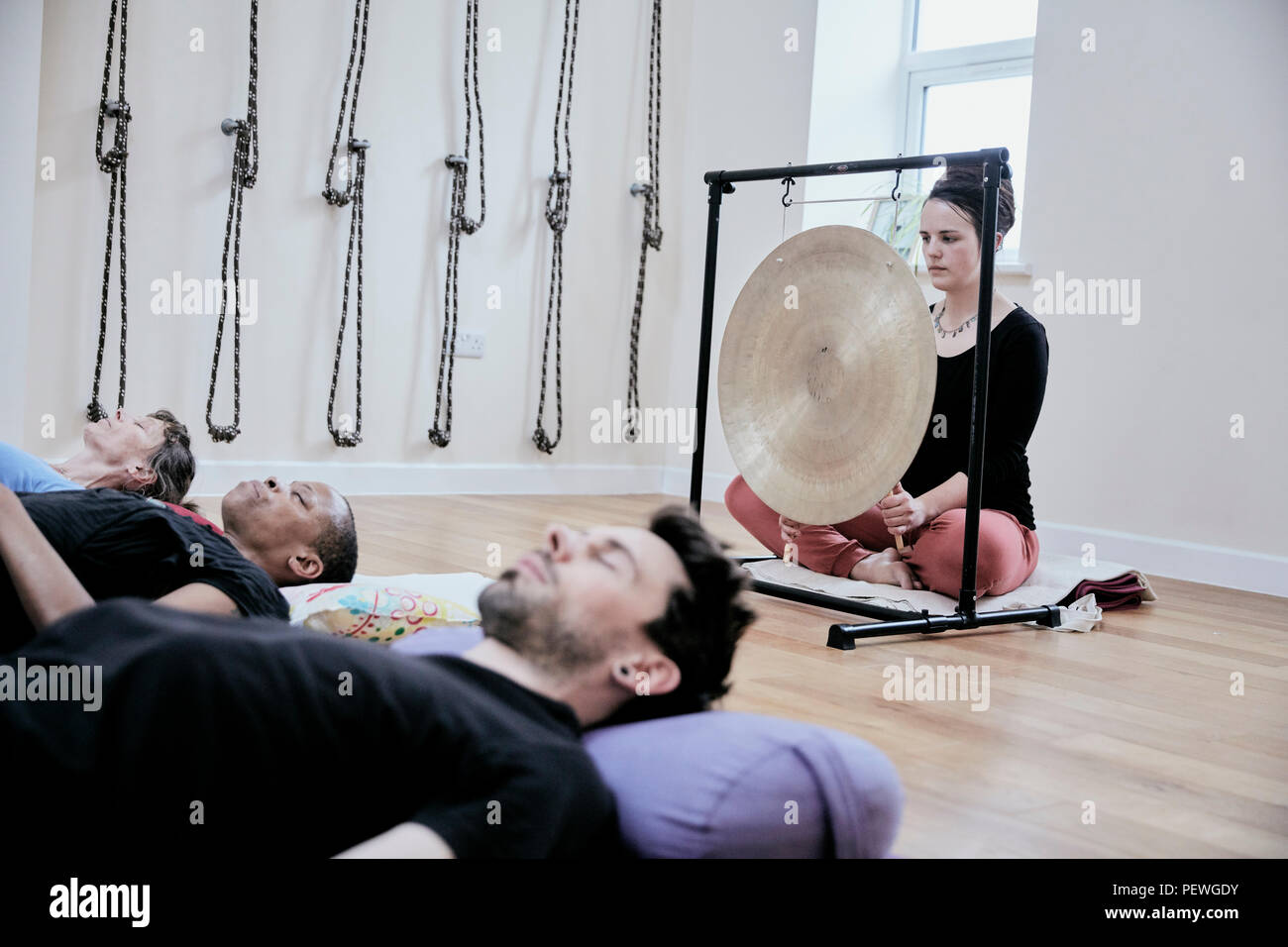 Woman using a gong during a sound therapy session and three people ...